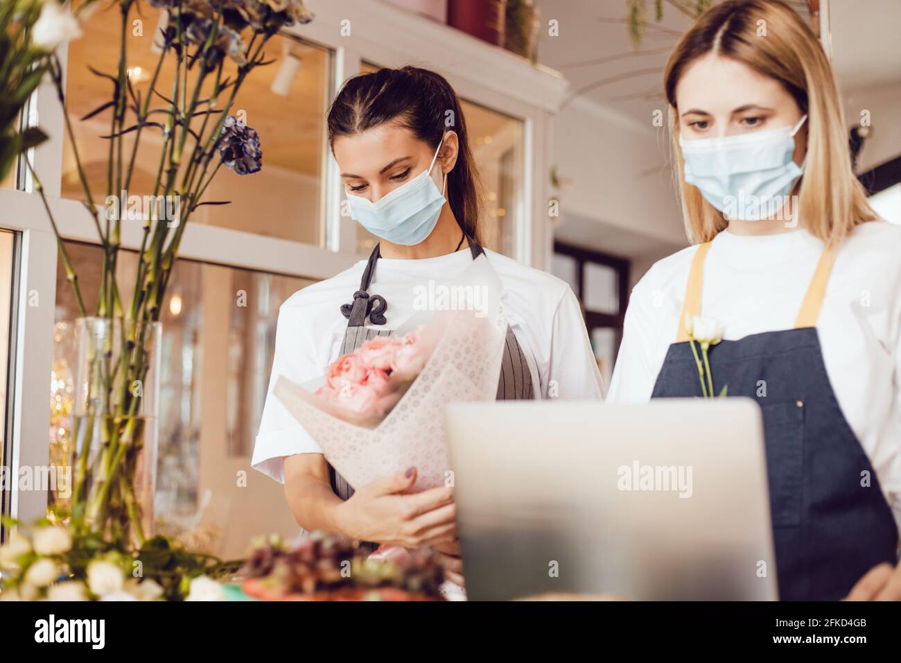 Flower shop workers in protective masks decorate a bouquet and use a ...