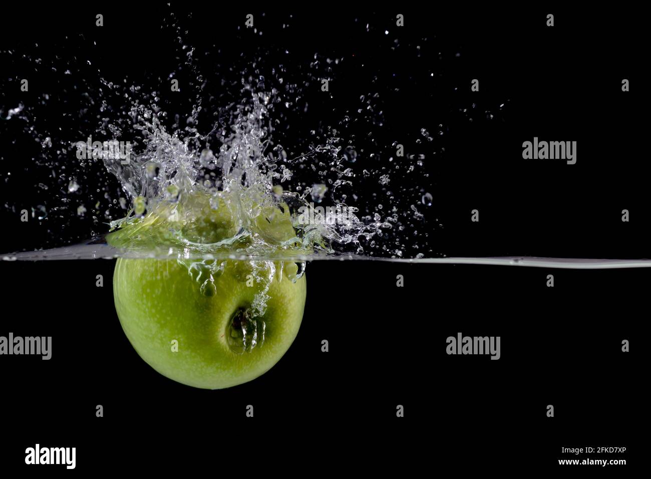Ripe green apple falling down into clear water with splashes against ...