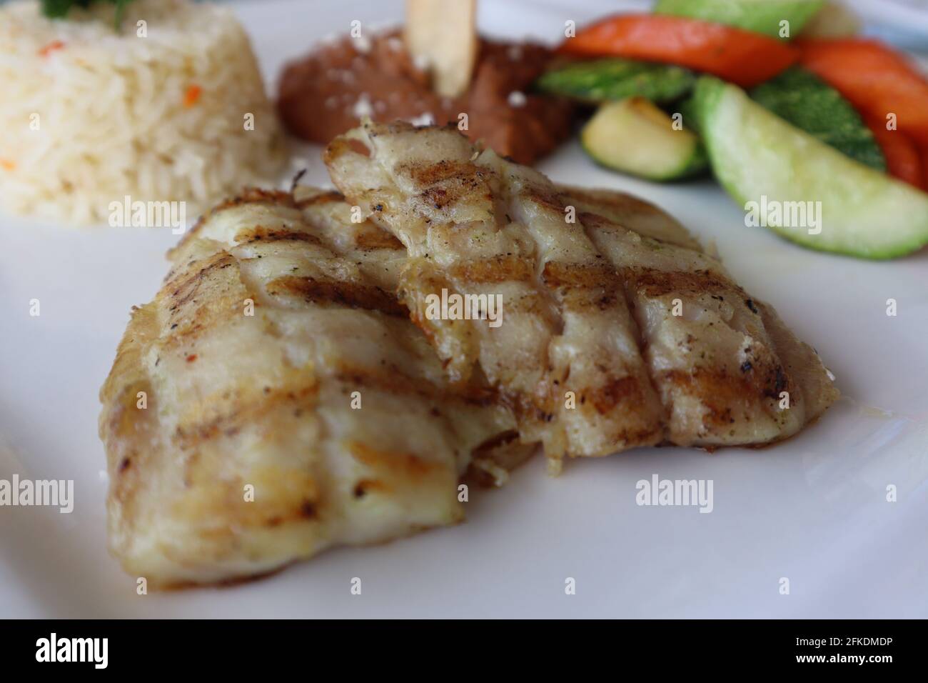 Closeup of grilled fish entree with rice pilaf and fresh vegetables ...