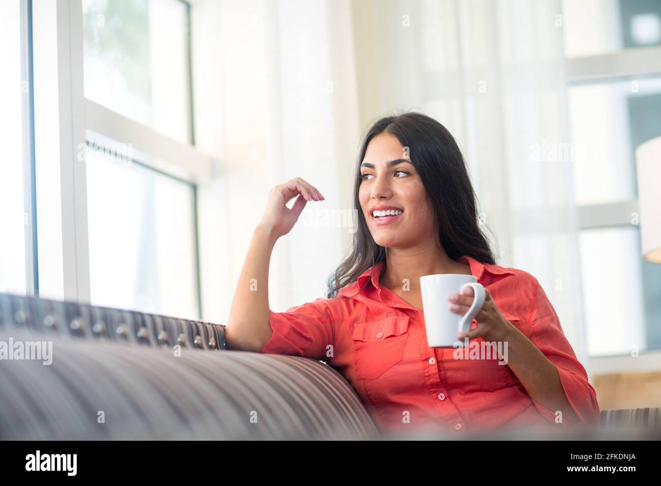 Young woman sitting on the sofa and smiling Stock Photo - Alamy