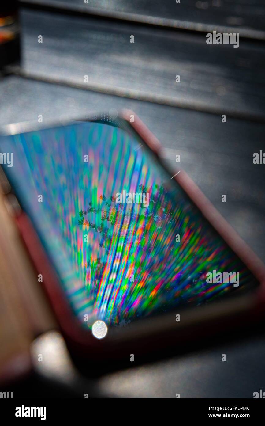 Bright rainbow rays reflect in mobile phone screen surface with dark ...