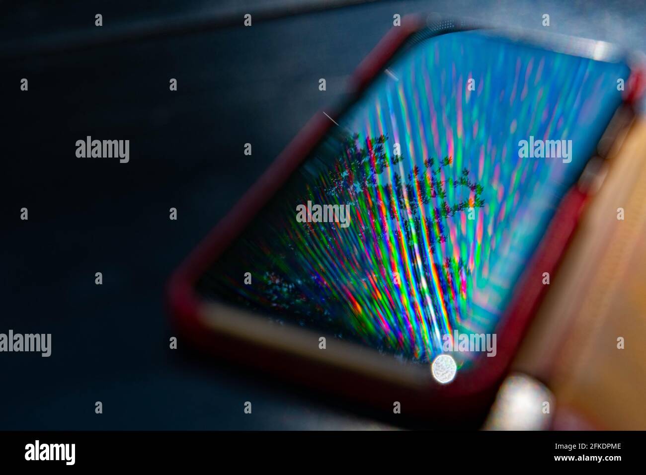 Bright rainbow rays reflect in mobile phone screen surface with dark ...