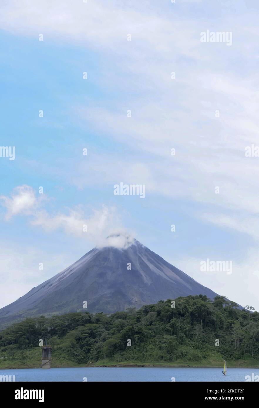 Vertical shot of the Arenal volcano peak and a lake with forests on the ...