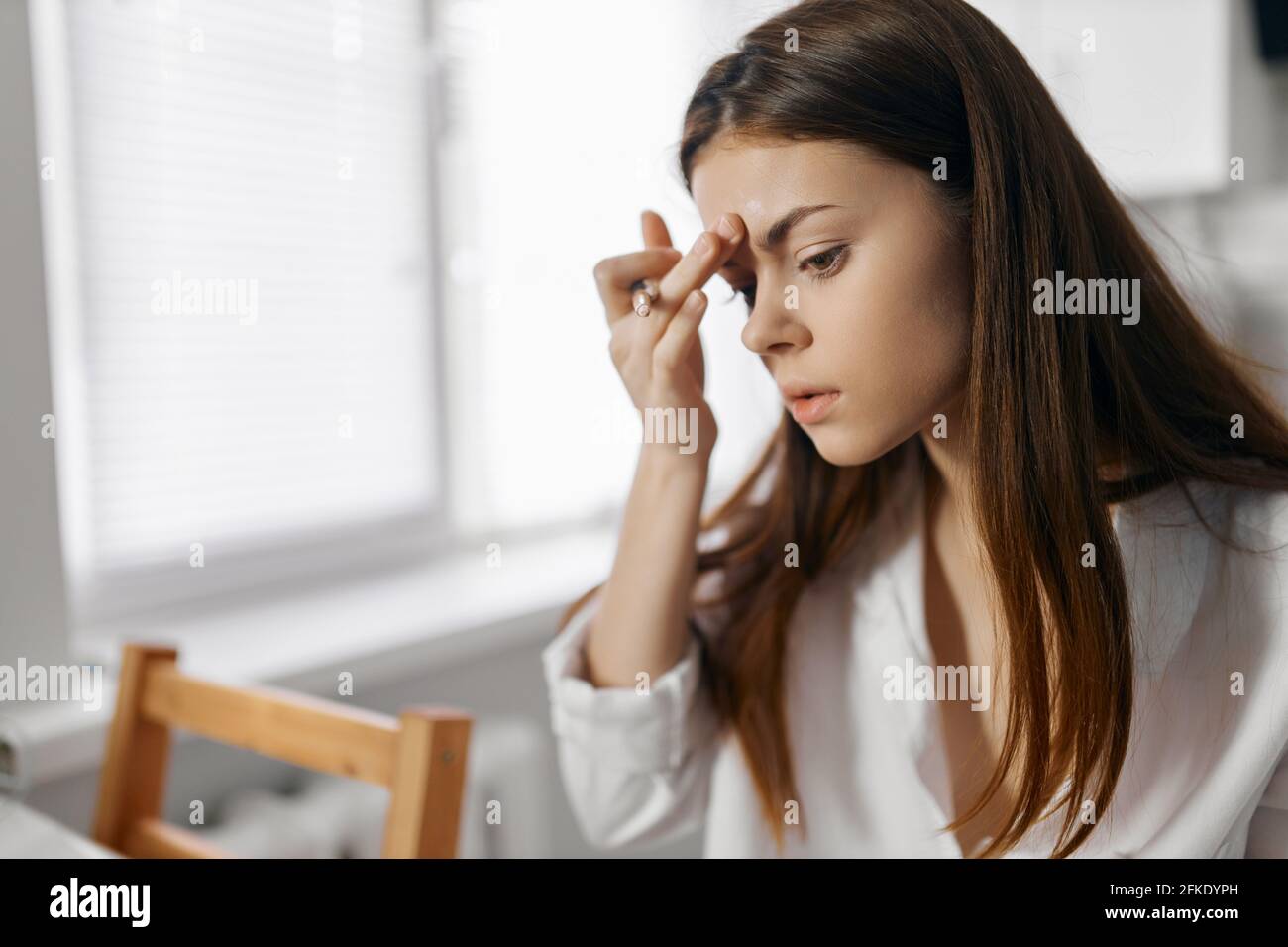woman touches her forehead with her hand in the kitchen at the table ...