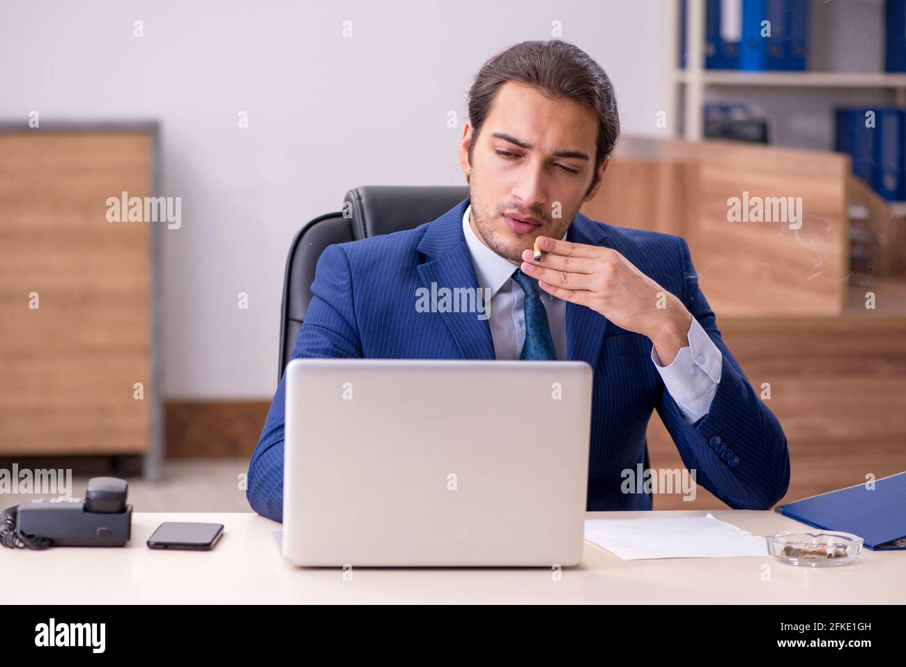 Young man employee smoking cigarettes in the office Stock Photo - Alamy