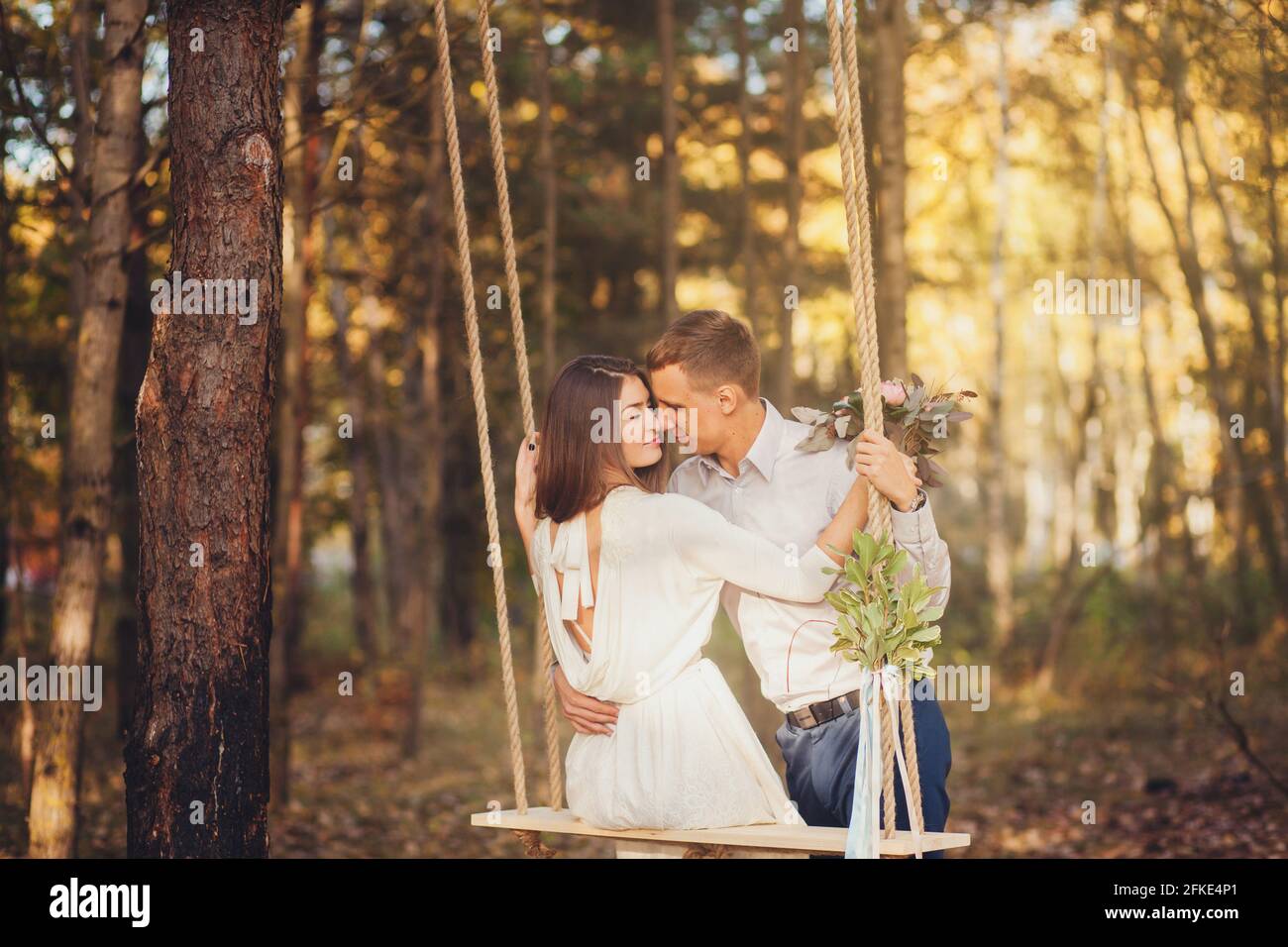 Romantic couple in a summer park. Man hugging a girl sitting on a swing ...