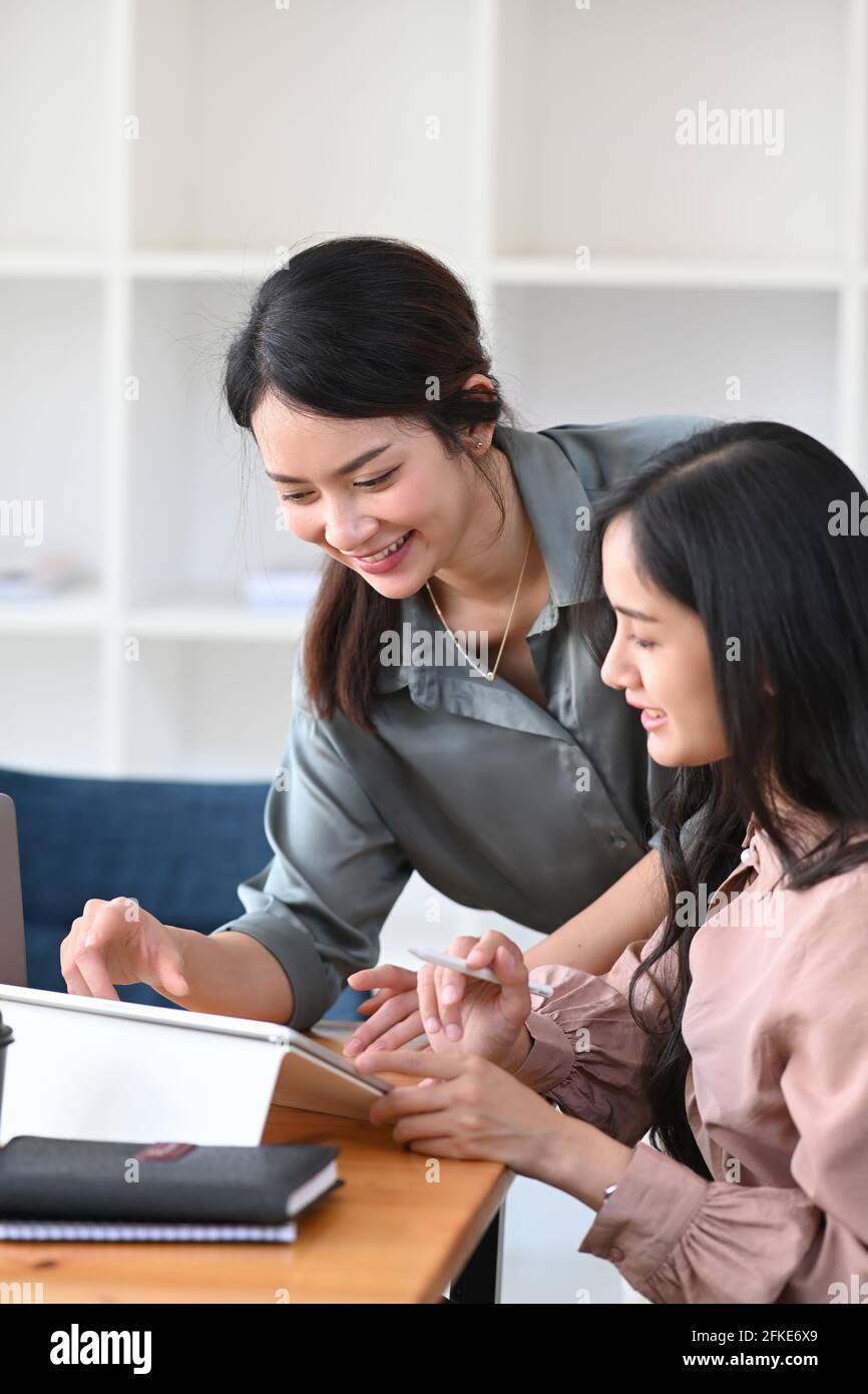 Smiling young female employee helping her colleague working in office ...