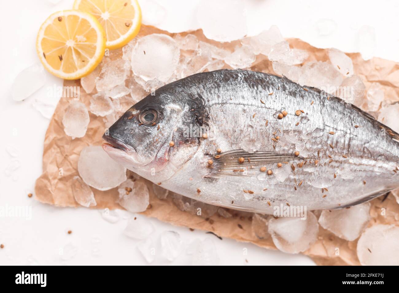 Raw dorada fish or gilt-head bream on ice with lemon and salt over ...