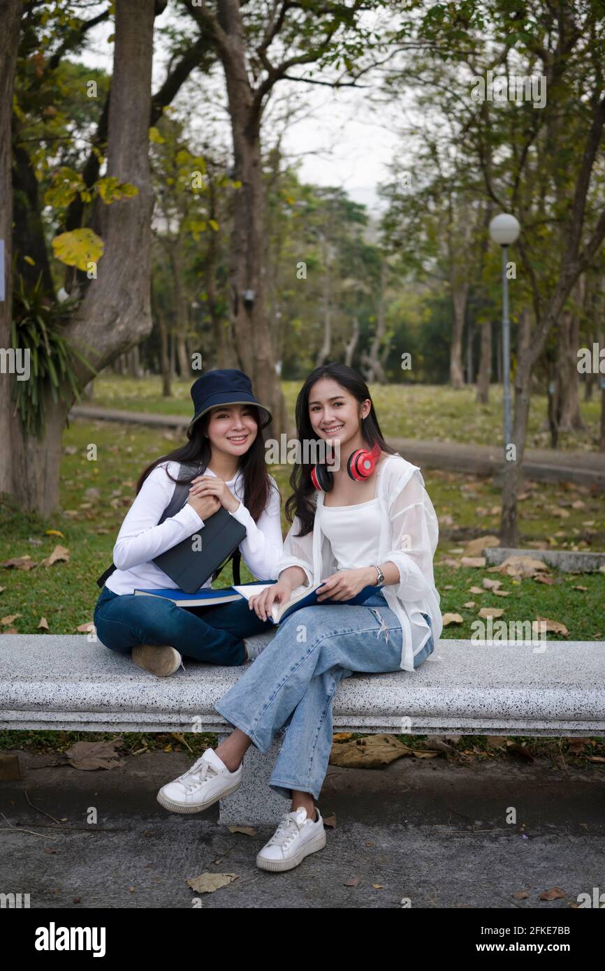 Two happy female college students sitting on bench and resting in ...
