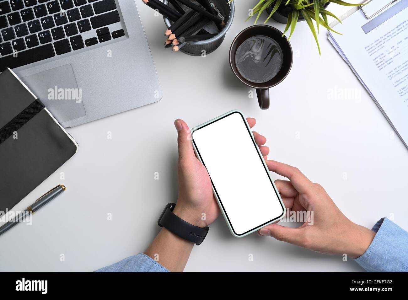 Businessman holding mobile phone with blank screen at white office desk ...