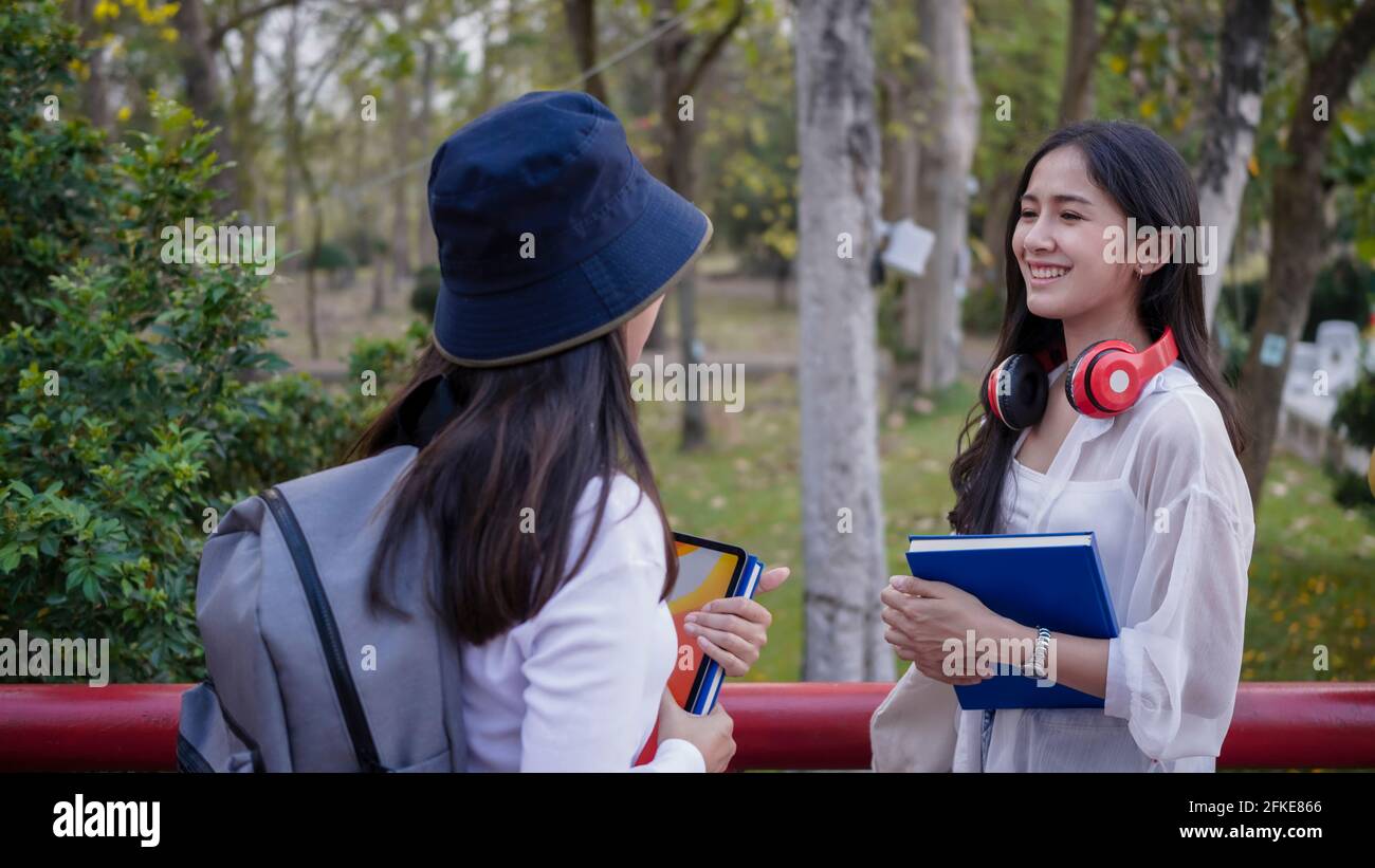 Two happy college students holding books and talking each other in ...