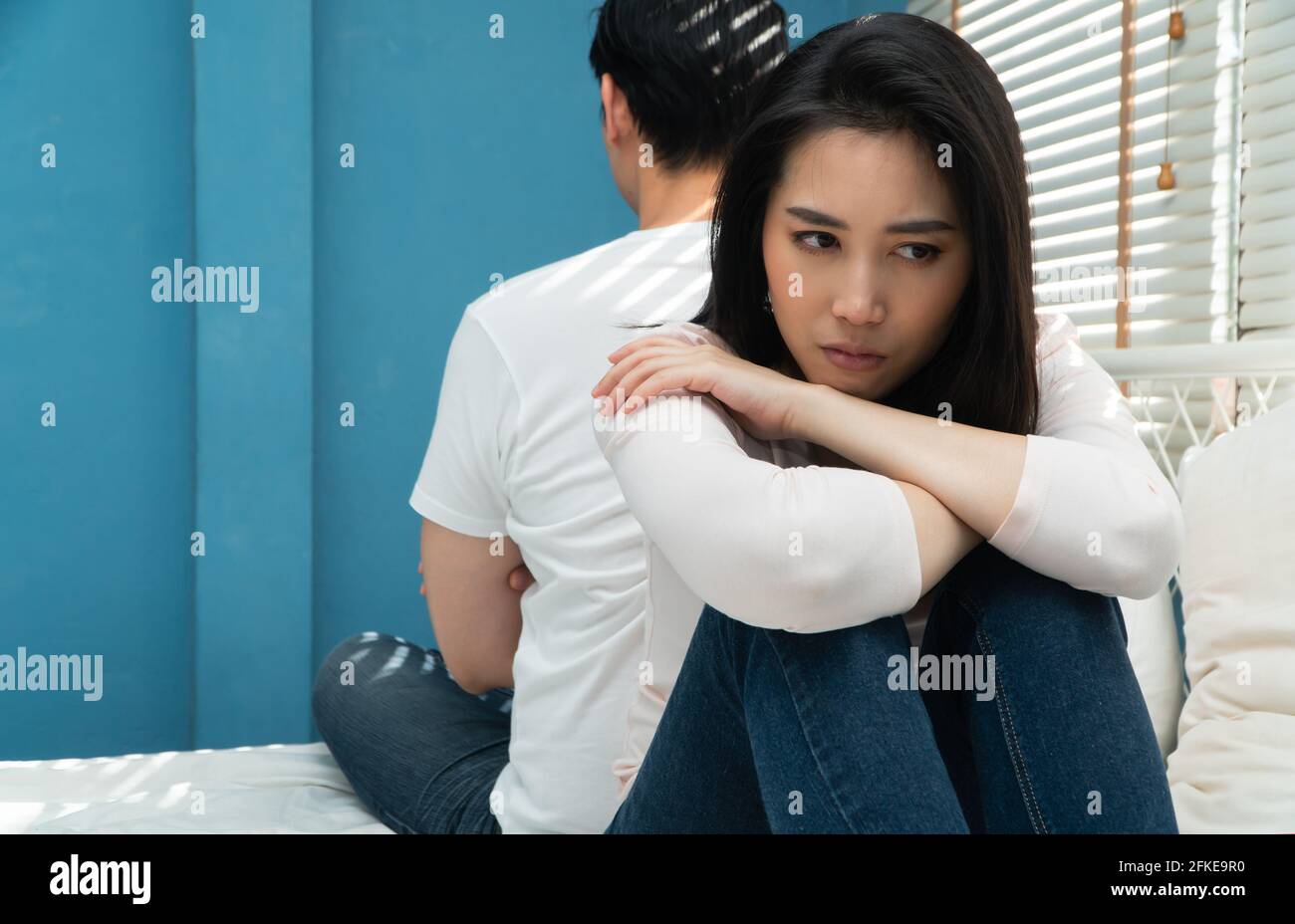 Unhappy Couples sitting behind each other on the bed and avoid talking ...