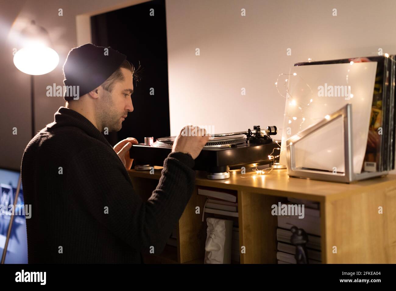 Young unshaven handsome hipster guy puts tonearm on vinyl record on ...