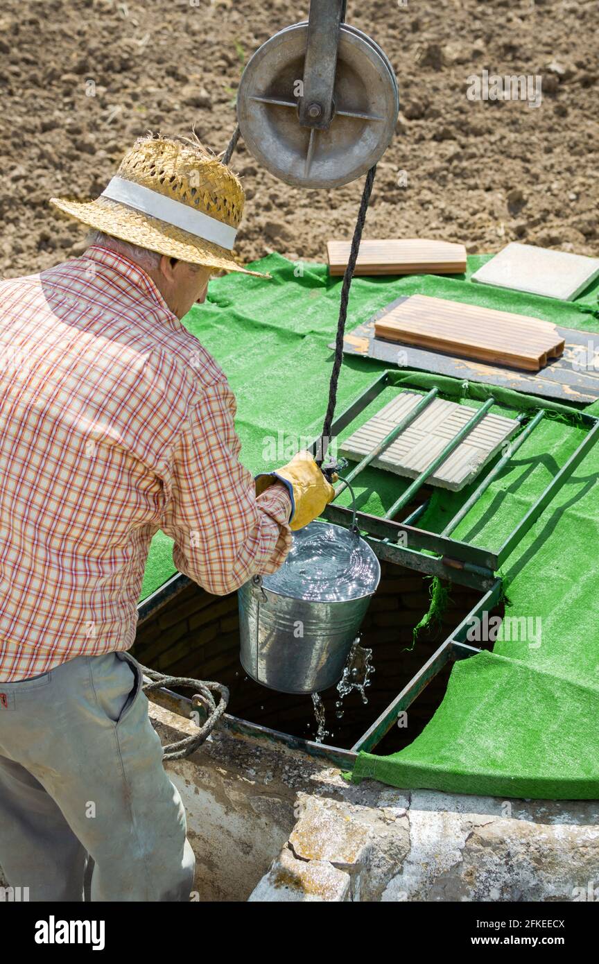 Old man drawing water from a rustic well with pulley in the countryside ...