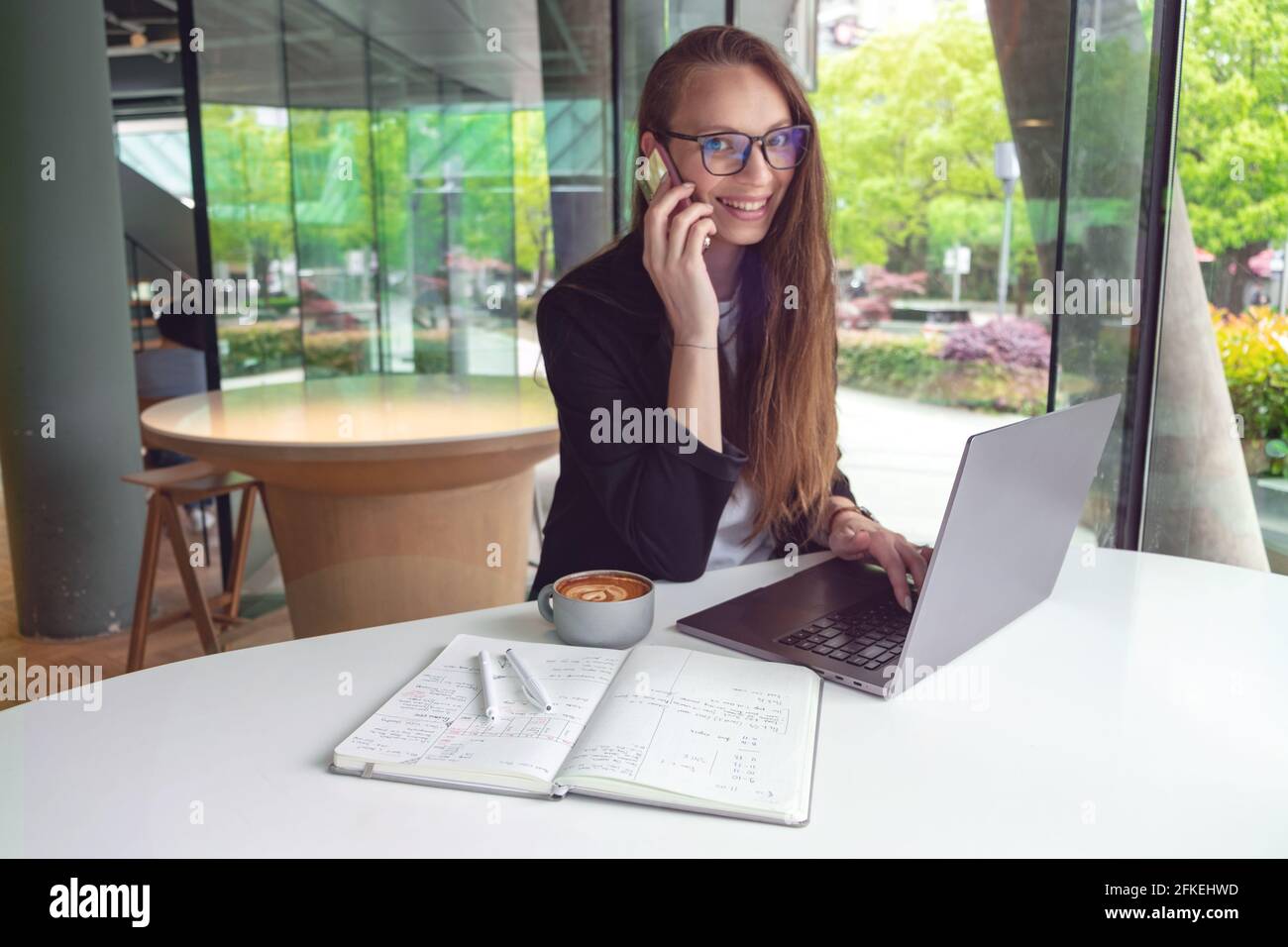 Beautiful lady is drinking coffee while working on a laptop in a coffee ...
