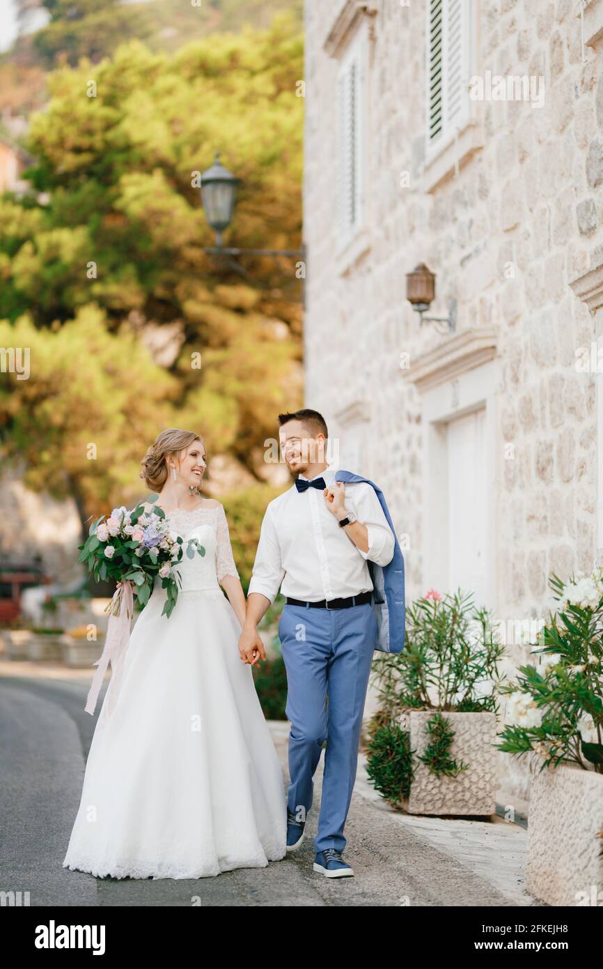 The bride and groom walk holding hands near a beautiful brick house in ...