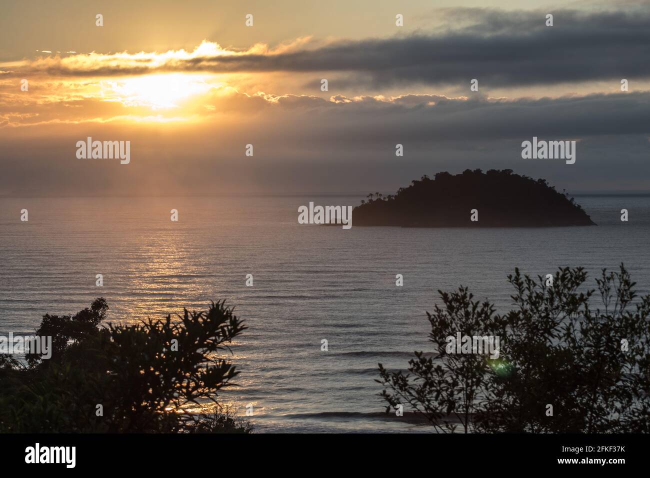 Rising sun over a distant island behind beautiful clouds Stock Photo ...