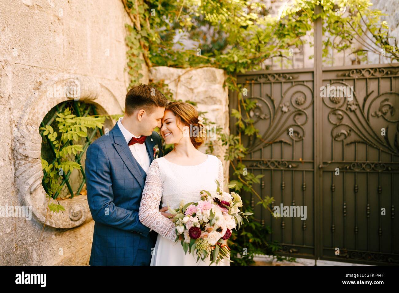 Smiling bride and groom hugging on the background of wrought iron gates ...