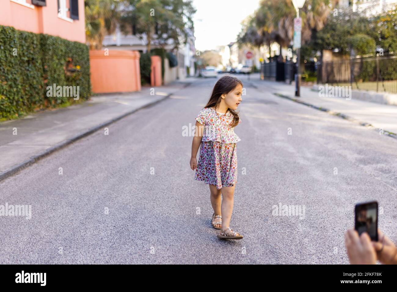 Happy little girl in flowered dress slowly walking in empty street ...