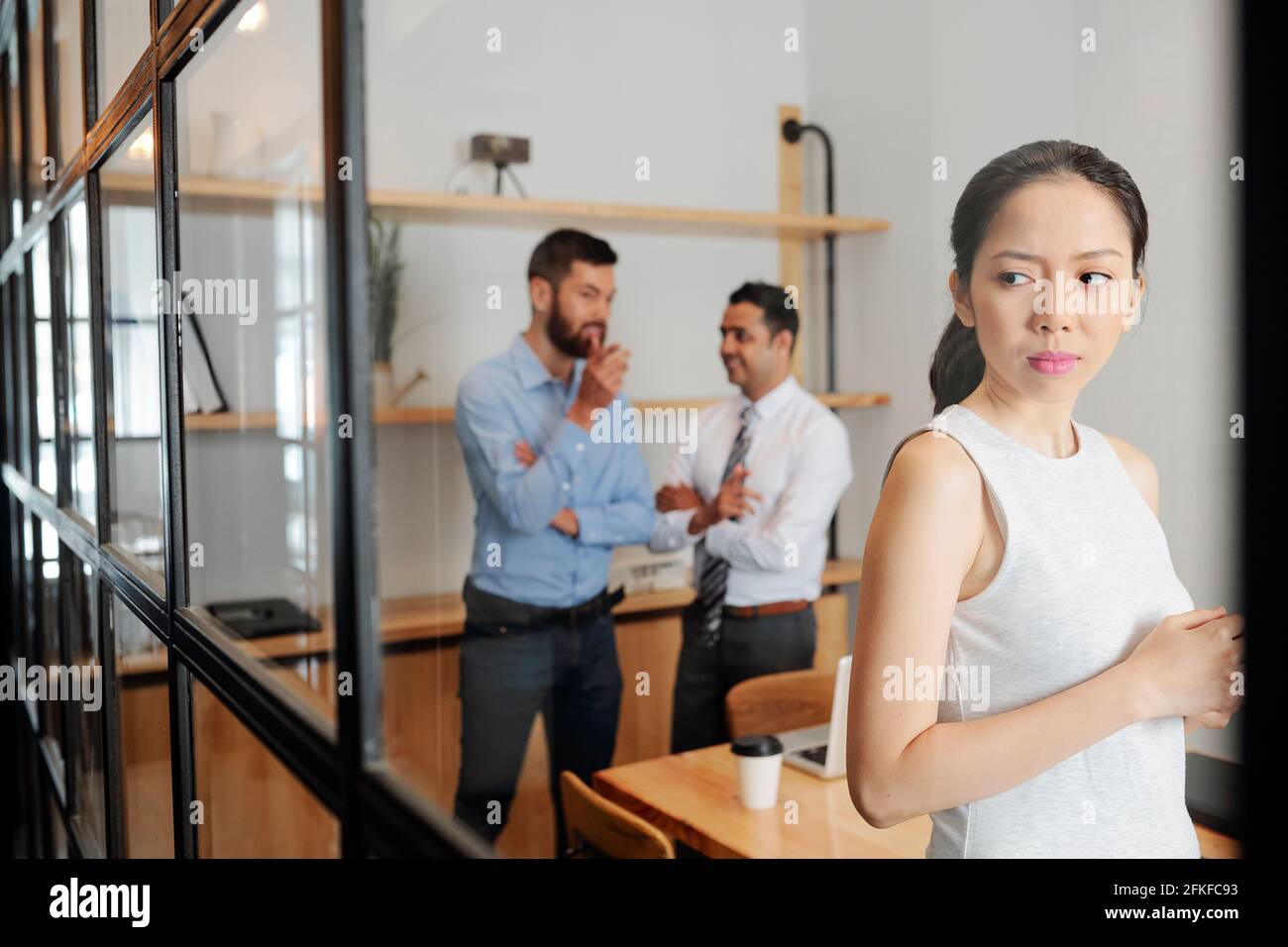Serious young businesswoman eavesdropping on conversation of her male ...