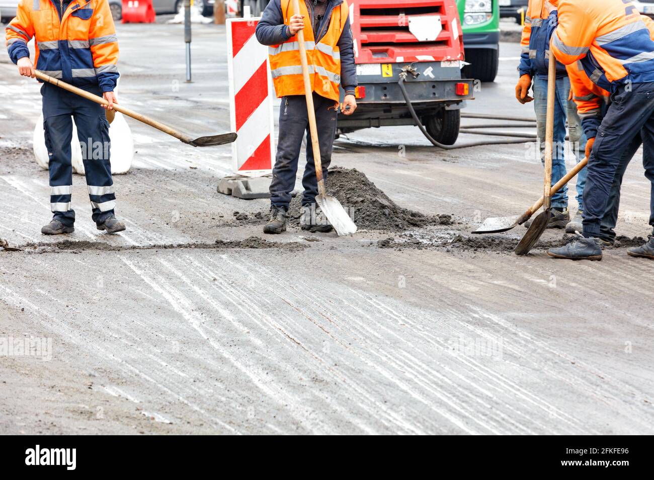 Road workers in orange overalls are cleaning the road with shovels in a ...
