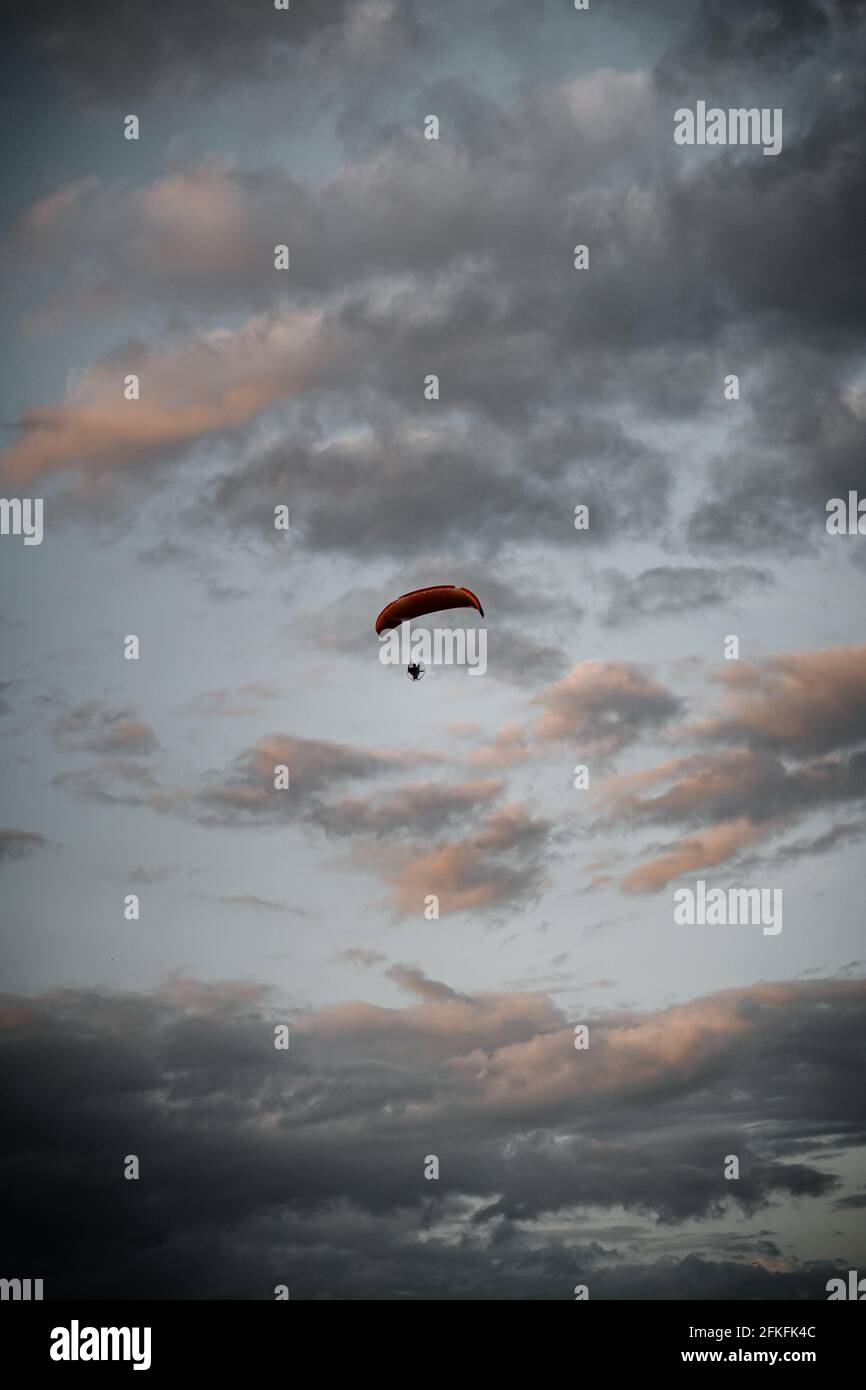 Vertical shot of a parachute flying high on a cloudy blue sunset sky ...