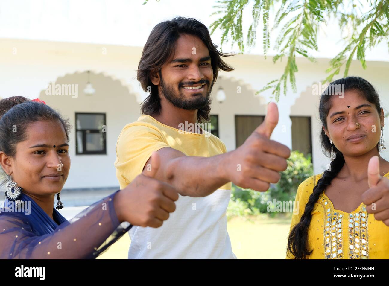 Group of cheerful young Indian friends standing outdoors showing thumbs ...