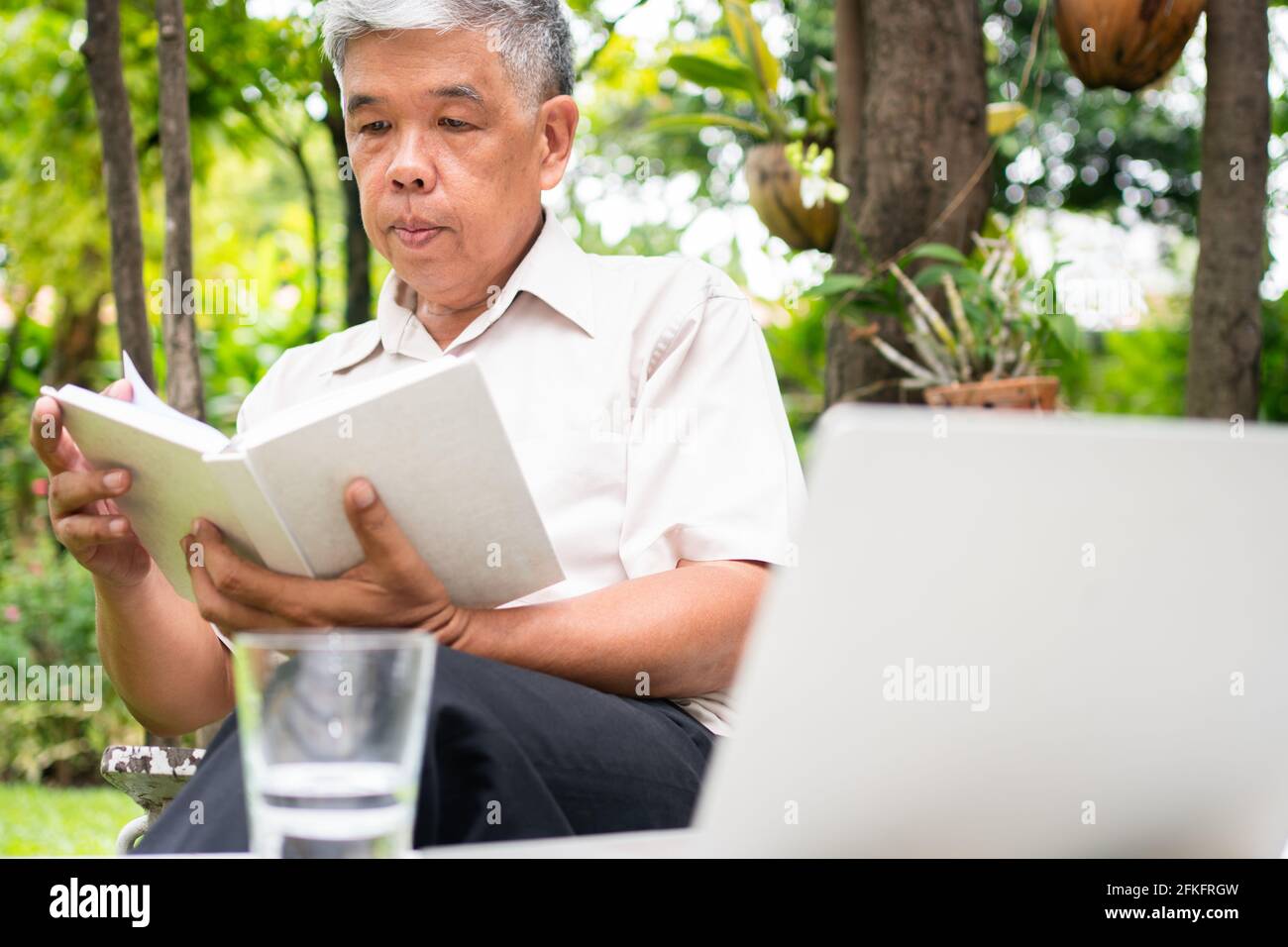 senior old man reading a book in the park and drinking water. Concept ...