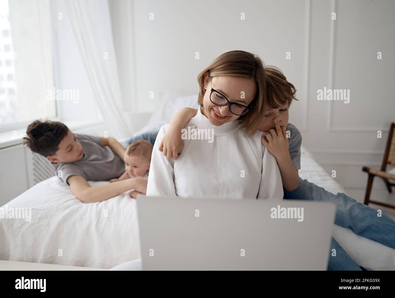 Busy caucasian woman trying to work while baby sitting three kids ...