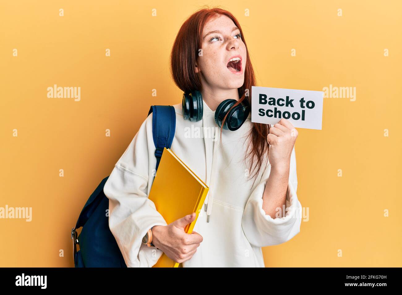 Young red head girl wearing backpack holding back to school banner ...