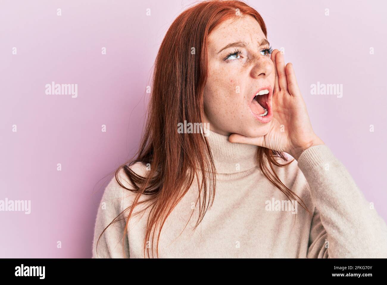 Young red head girl wearing turtleneck sweater shouting and screaming ...