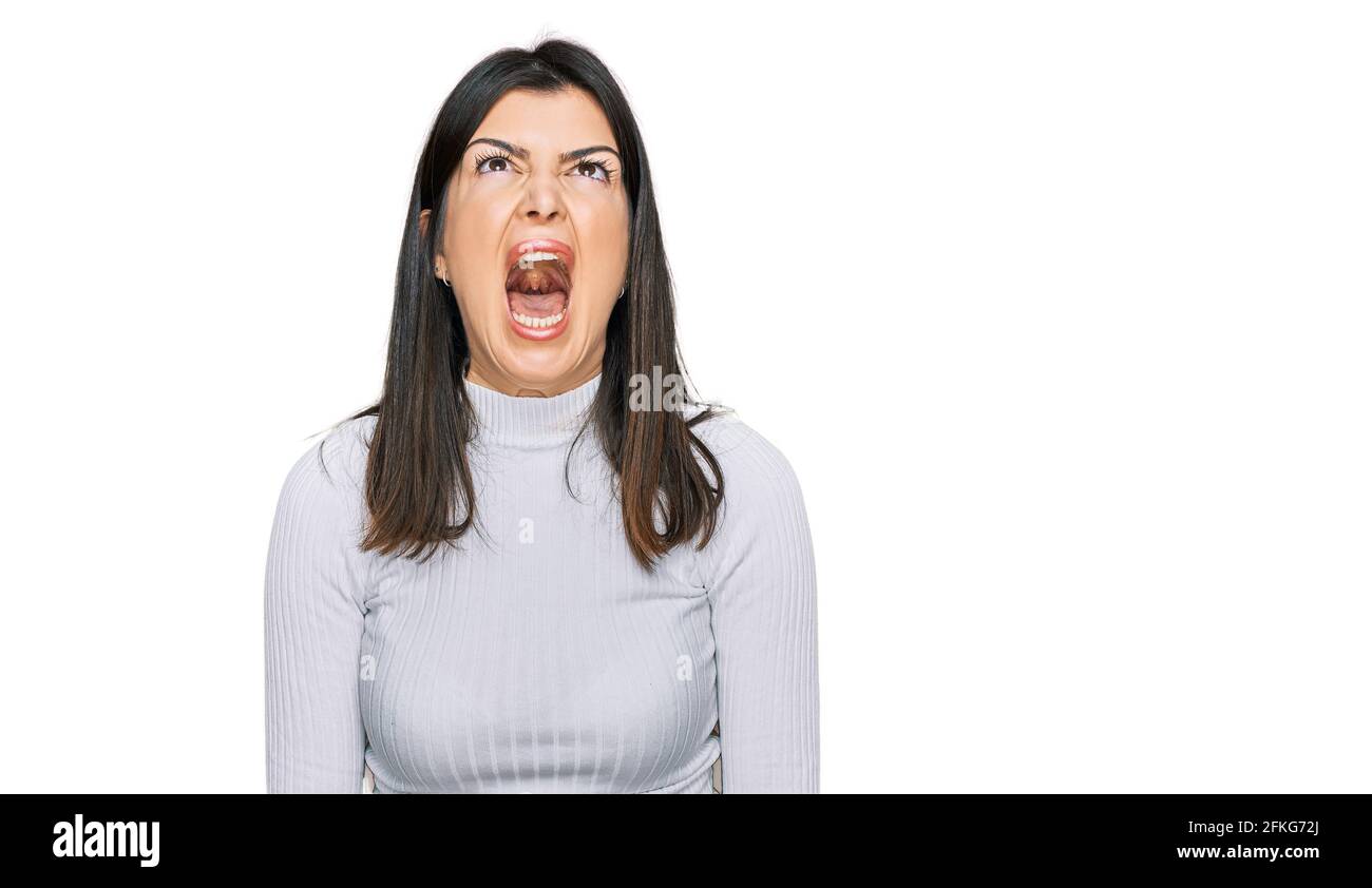 Beautiful brunette woman wearing casual clothes angry and mad screaming ...