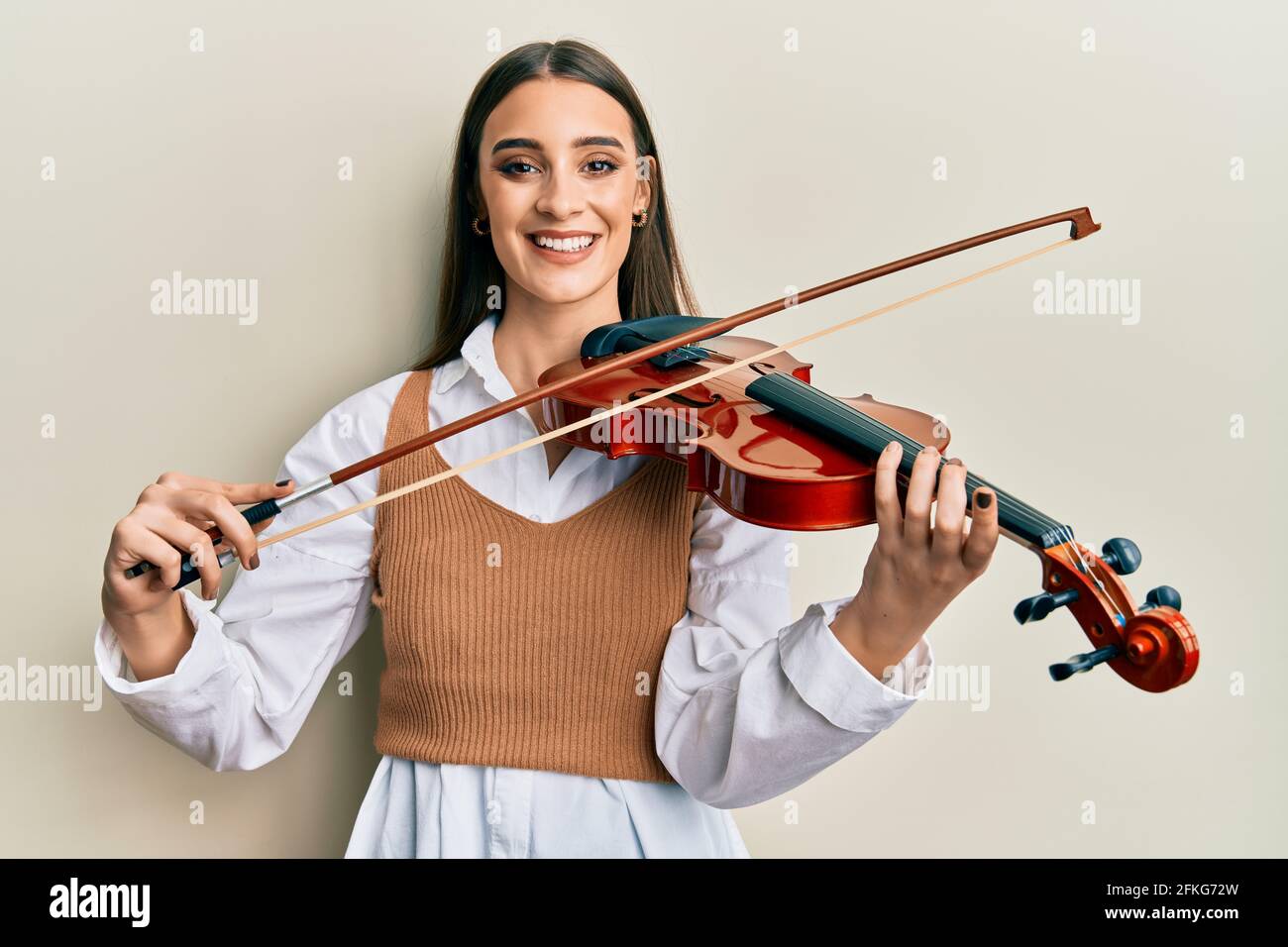 Beautiful brunette young woman playing violin smiling with a happy and ...