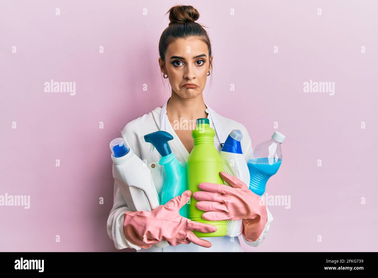 Beautiful brunette young woman wearing cleaner apron holding cleaning ...