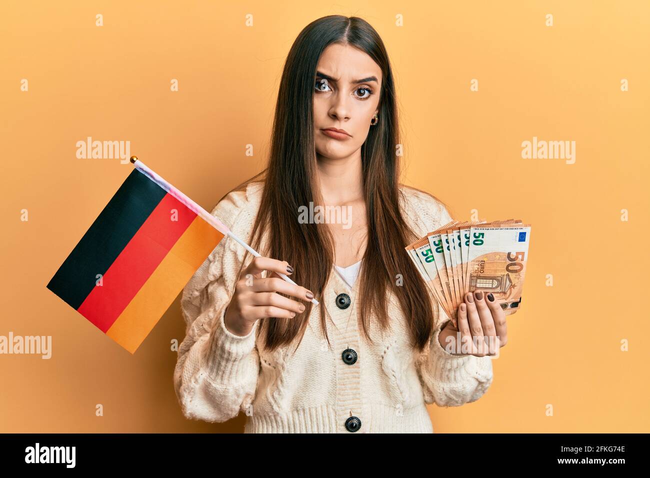 Beautiful brunette young woman holding germany flag and euros banknotes ...