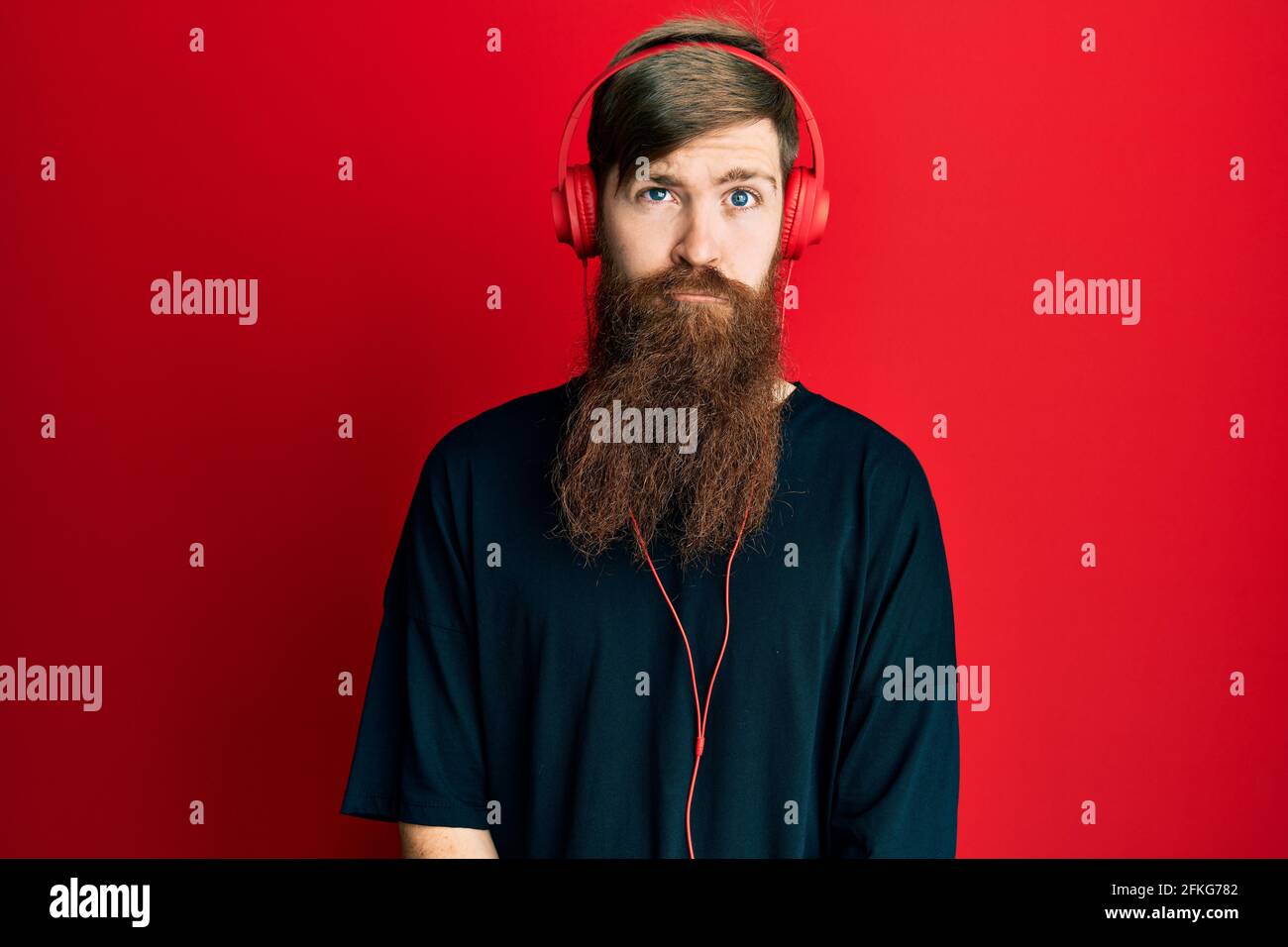 Redhead man with long beard listening to music using headphones ...