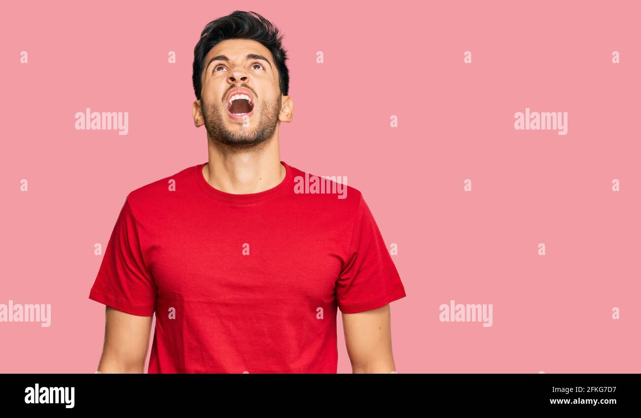 Young handsome man wearing casual red tshirt angry and mad screaming ...