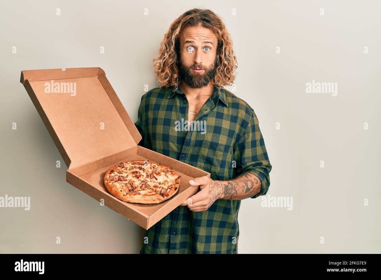Handsome man with beard and long hair holding italian pizza in shock ...