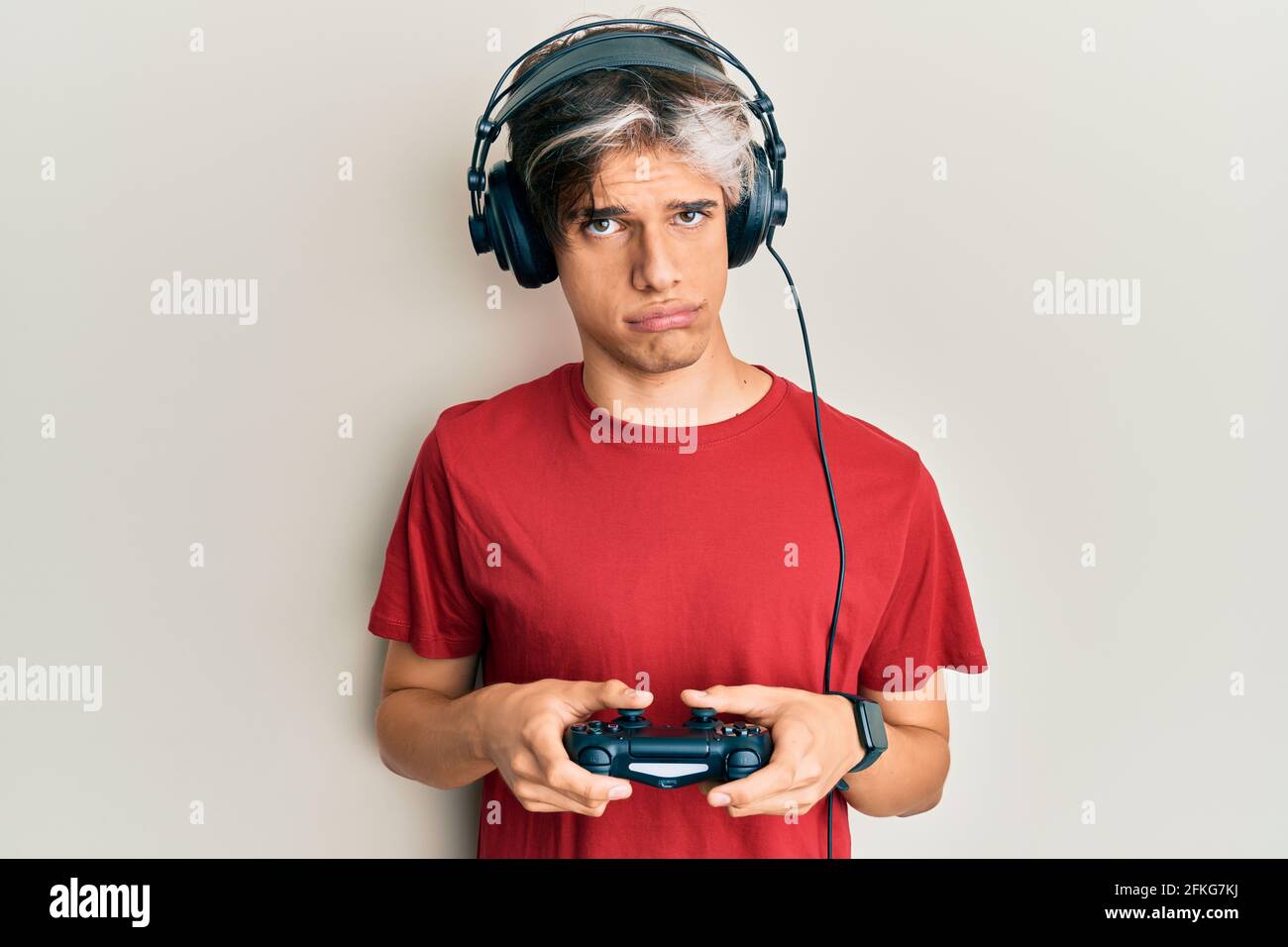 Young hispanic man playing video game holding controller depressed and ...