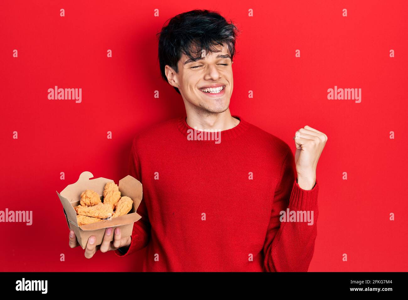 Handsome hipster young man eating chicken wings screaming proud ...