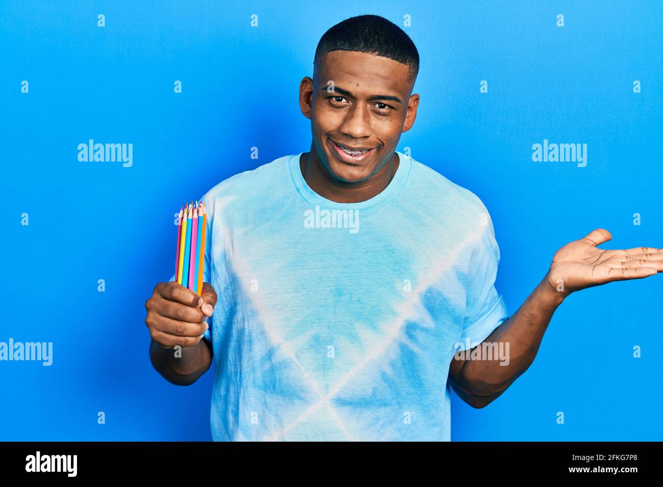 Young black man holding colored pencils celebrating achievement with ...