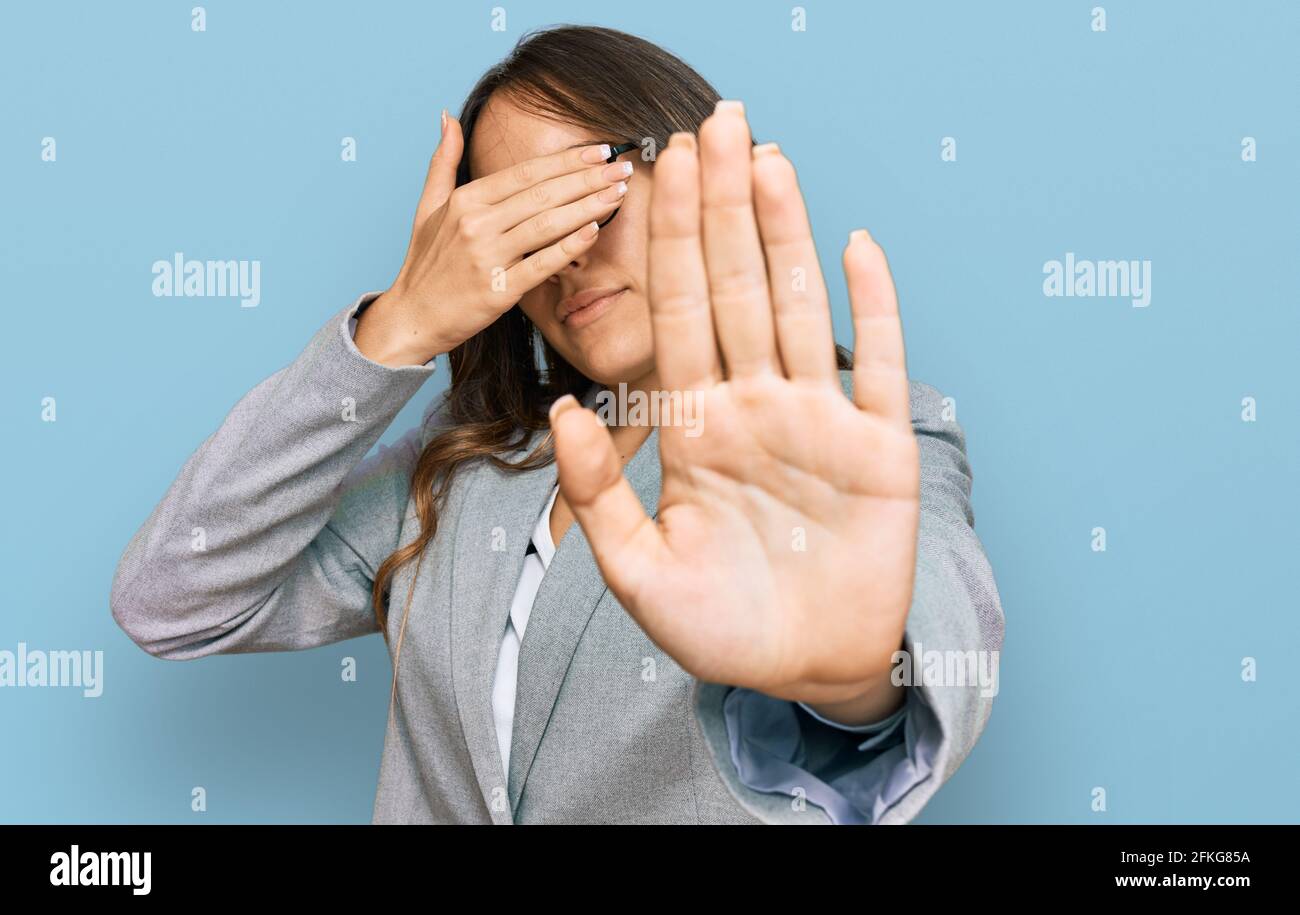 Young brunette woman wearing business clothes covering eyes with hands ...