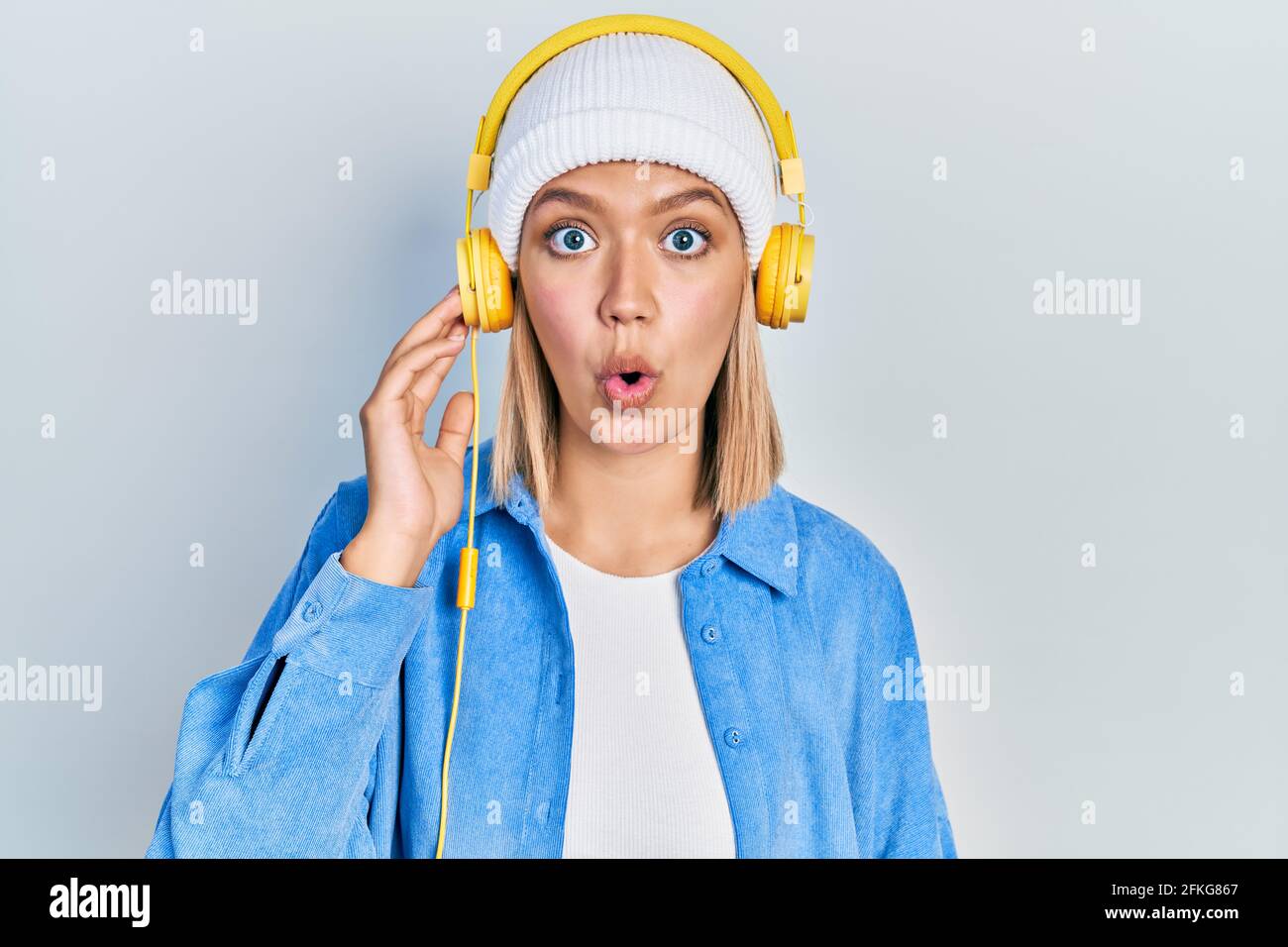 Beautiful blonde woman listening to music using headphones scared and ...