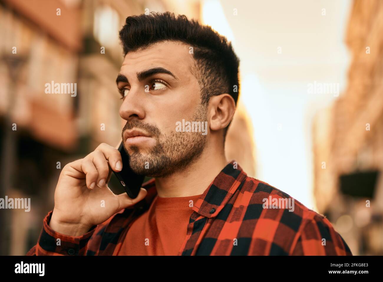 Young hispanic man with serious expression talking on the smartphone at ...