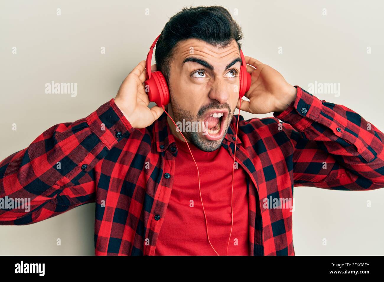 Young hispanic man listening to music using headphones angry and mad ...