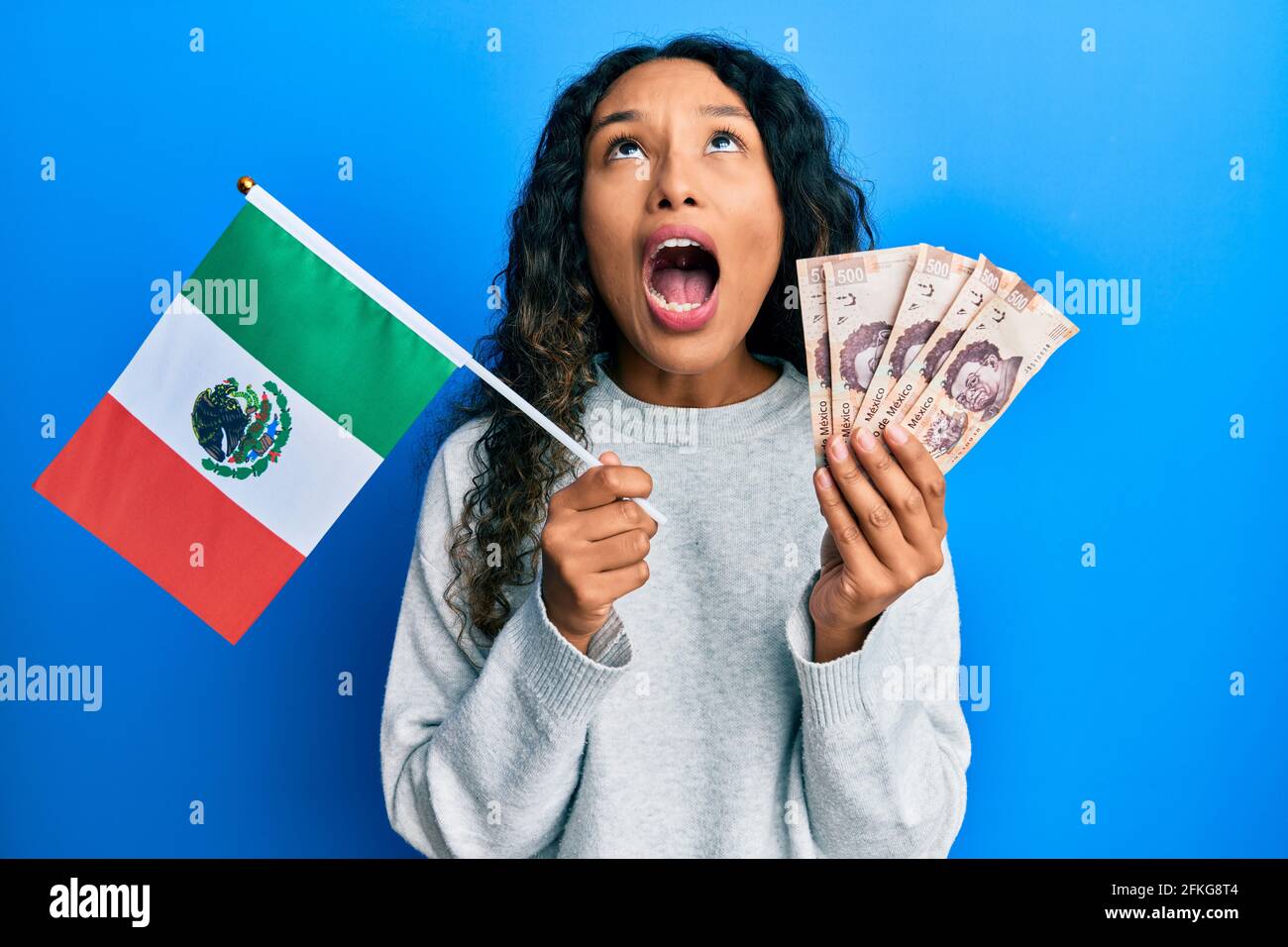 Young latin woman holding mexico flag and mexican pesos banknotes angry ...
