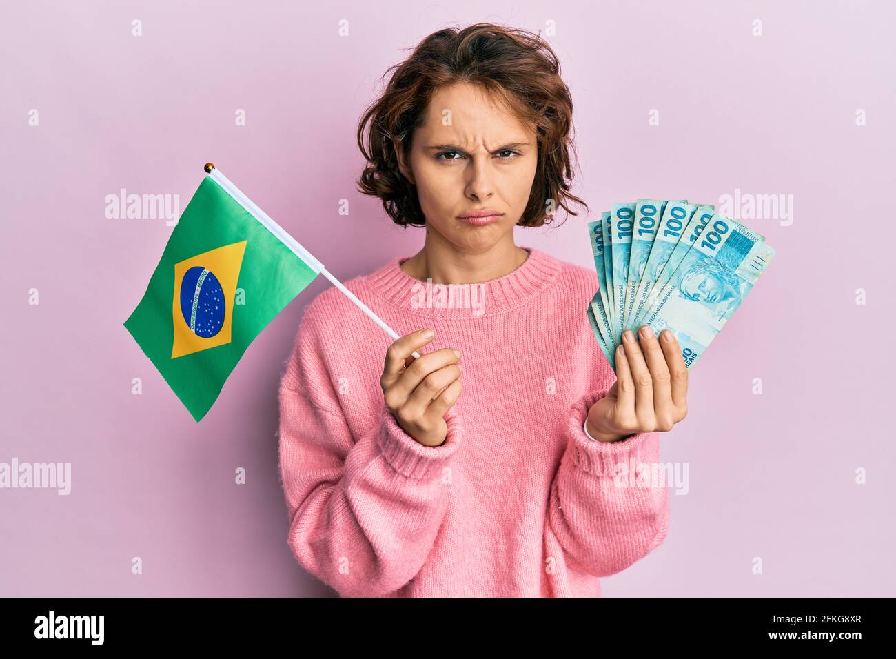 Young brunette woman holding brazil flag and real banknotes depressed ...