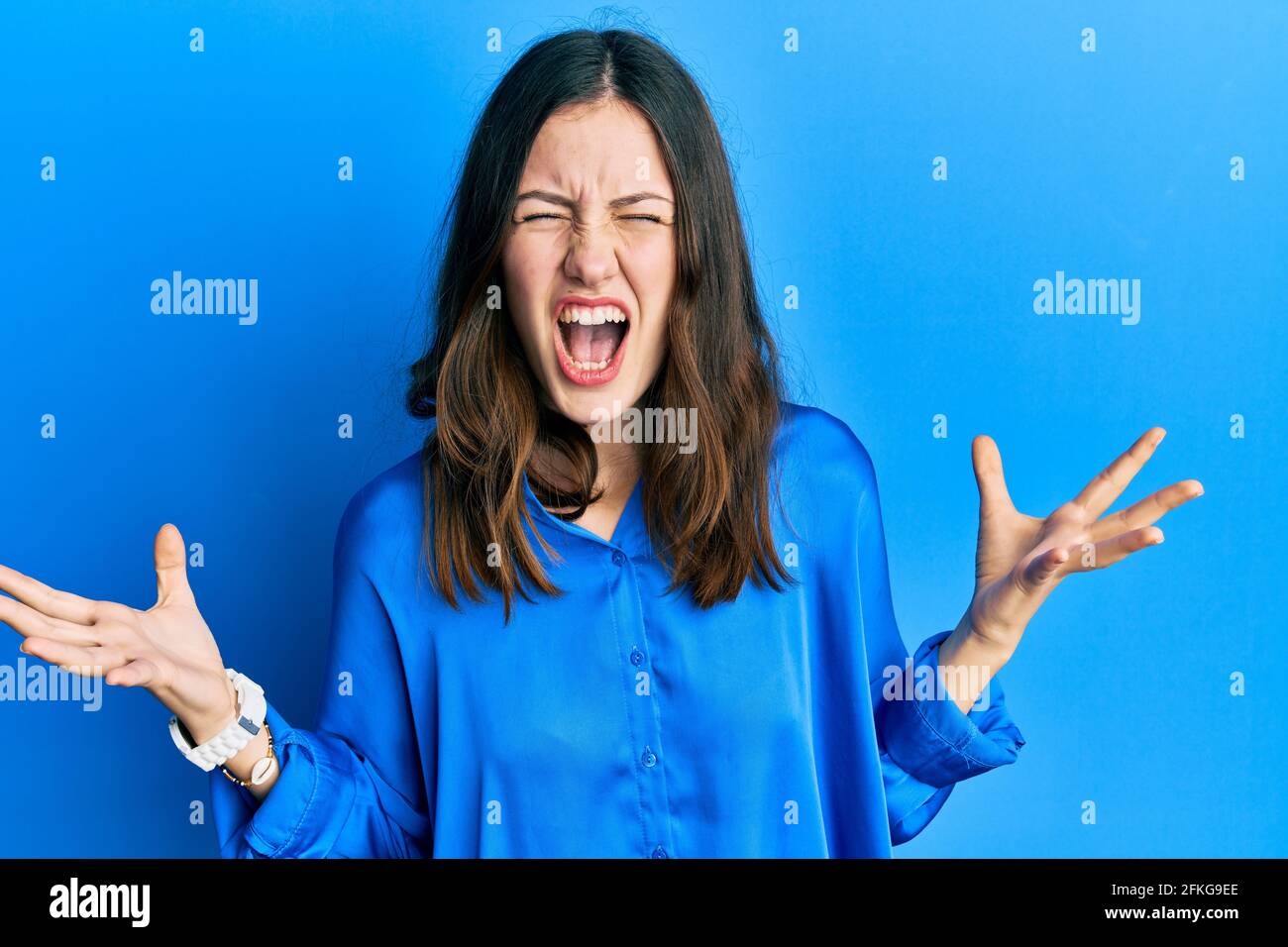 Young brunette woman wearing casual blue shirt crazy and mad shouting ...
