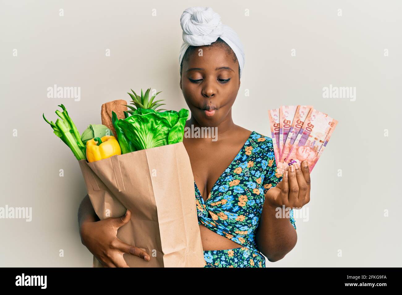 Young african woman holding groceries and 50 rand banknotes making fish ...