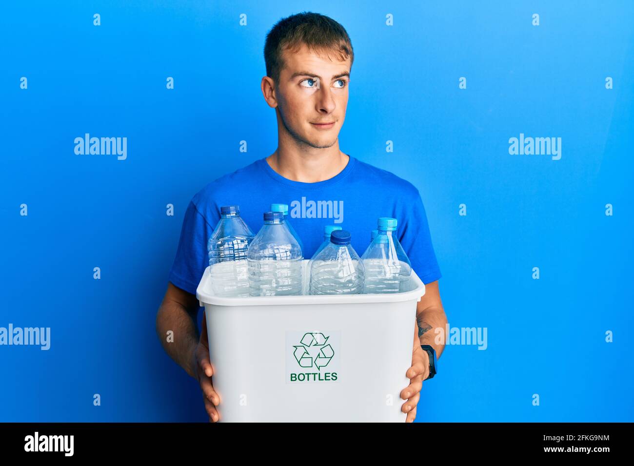 Young caucasian man holding recycling wastebasket with plastic bottles ...